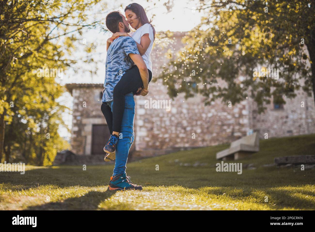 Full body side view of happy young man carrying girlfriend near green ...