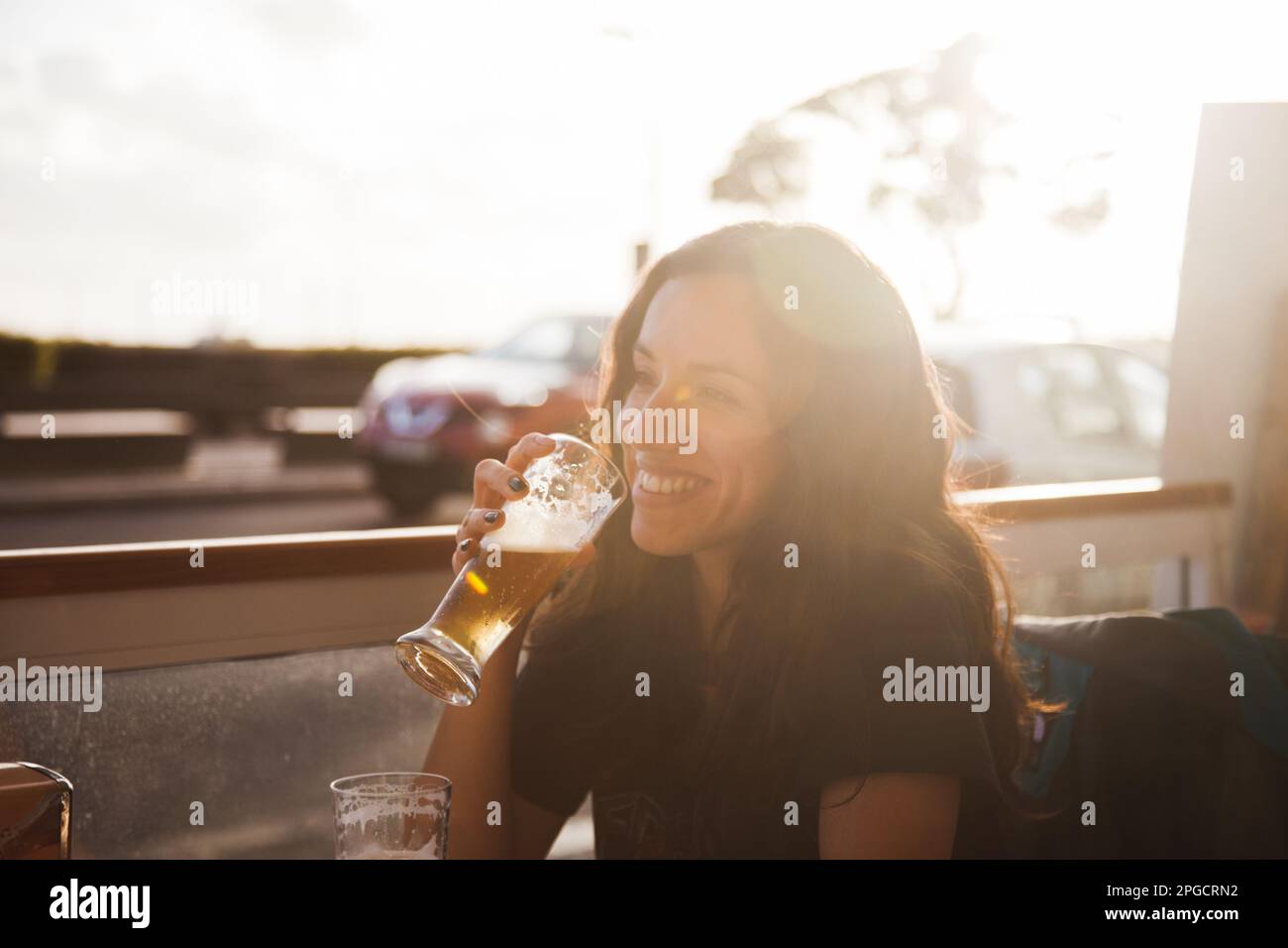 Positive young female in casual clothes smiling and drinking cold beer ...