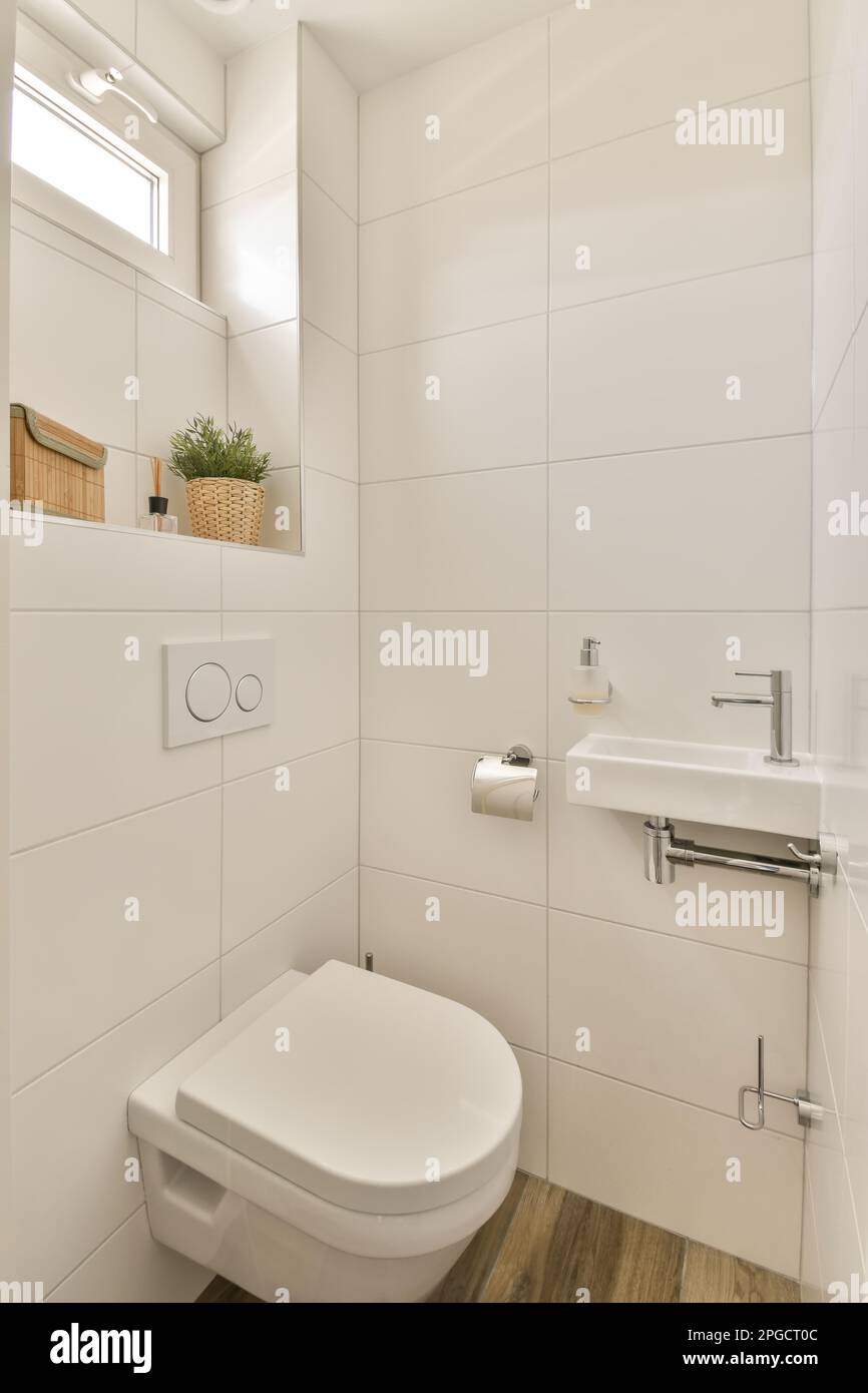 Interior of white tiled modern toilet with water closet and sink with ...