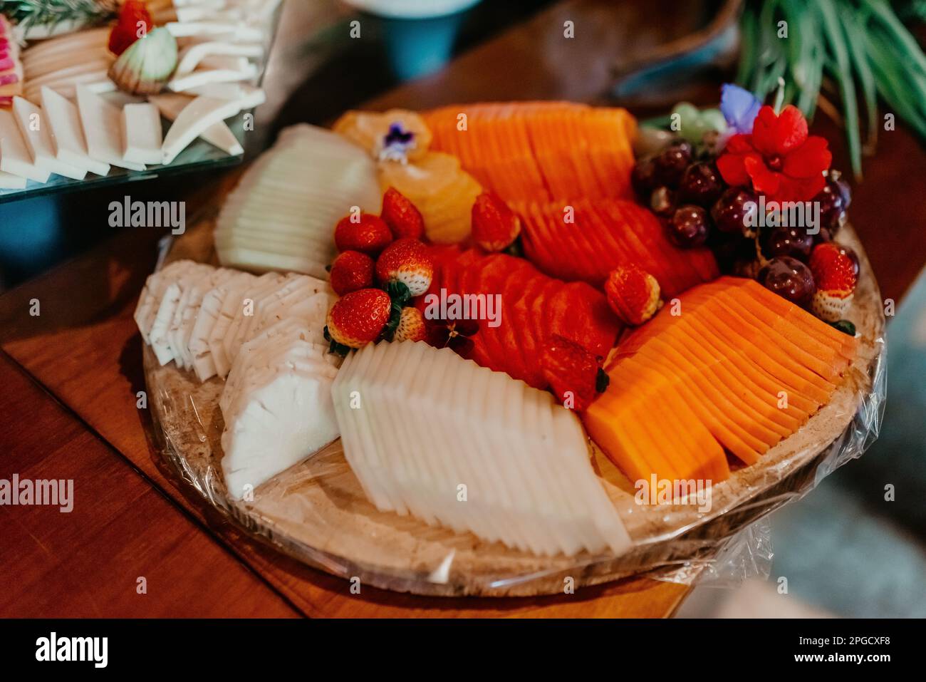 A wooden dining table display of assorted fruits and cheeses, with a ...