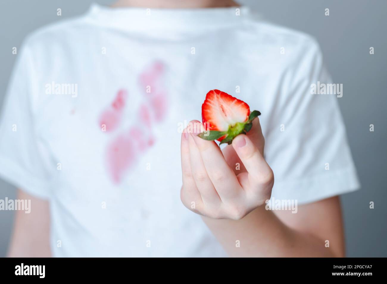 Close up child's hand holding a slice strawberry. Dirty stain on white ...