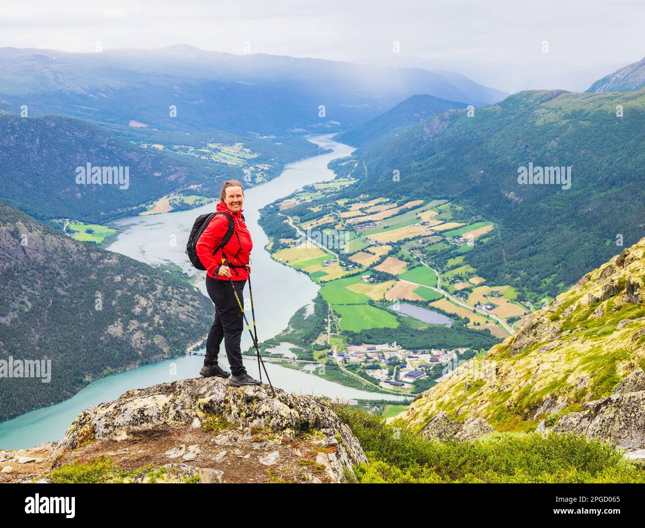 An active woman stands atop a mountain ridge in Norway, taking in the ...