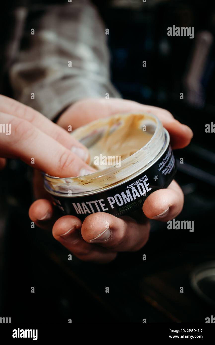 A closeup of the barber's hand holding a matte hair pomade container ...
