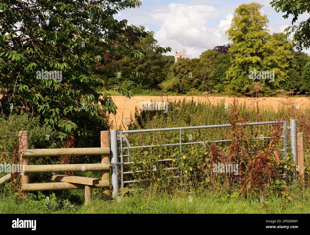 A field gate and footpath stile looking towards the tower of St Peter's ...