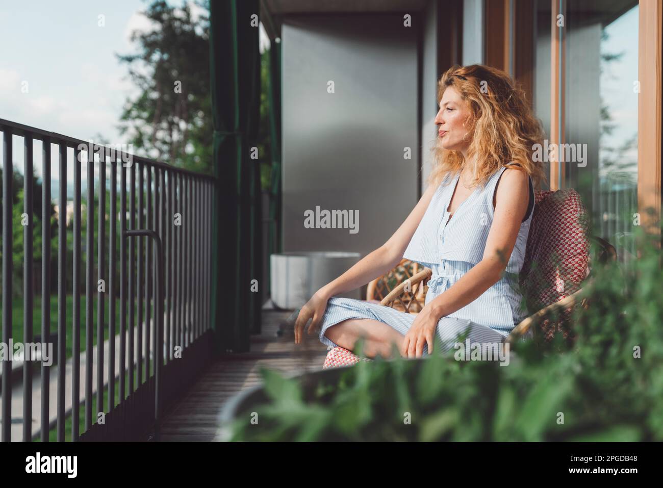 Side view of a woman relaxing on the balcony sitting in an armchair ...