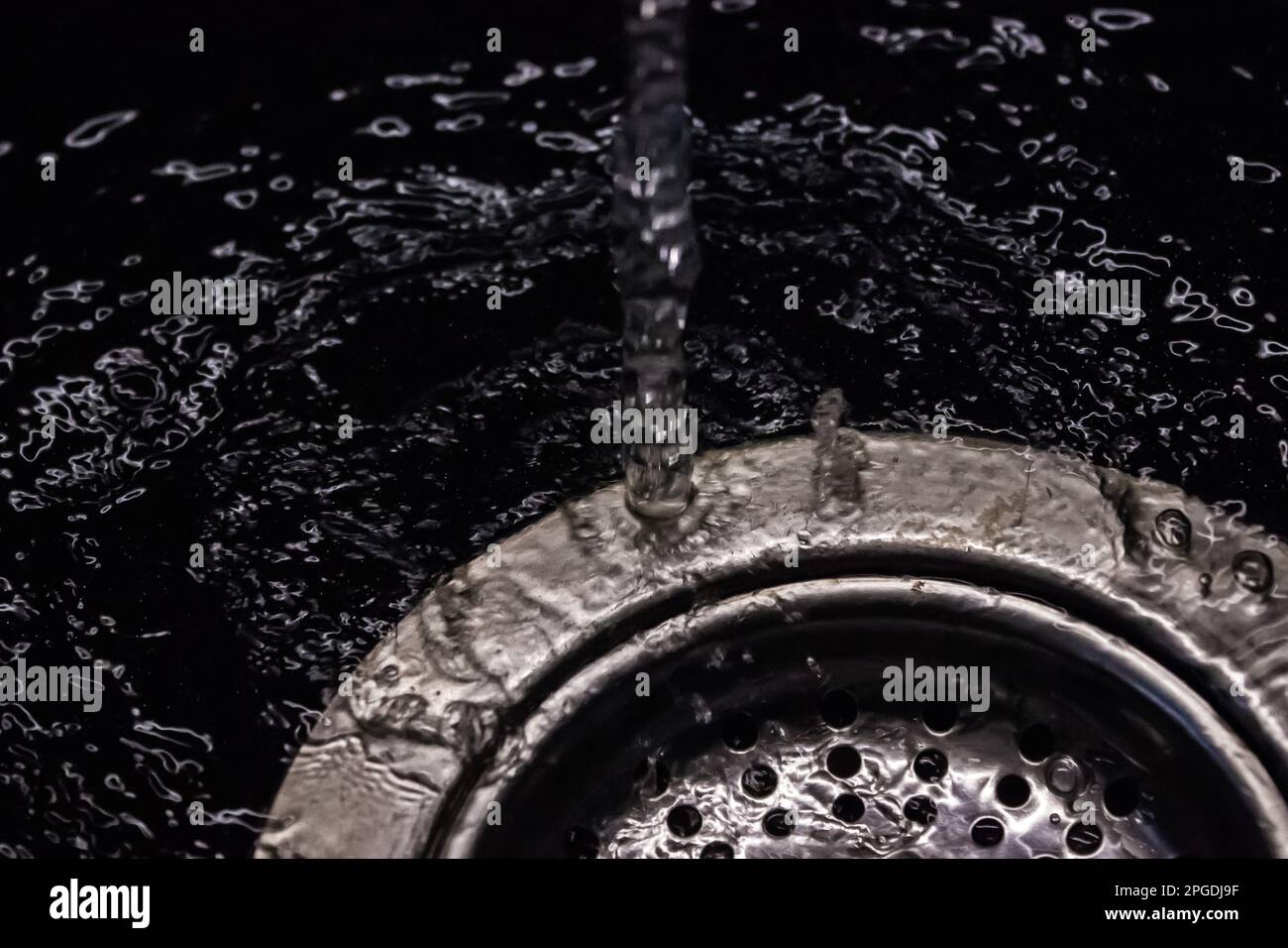 A high-resolution photograph of an empty black sink with a running ...