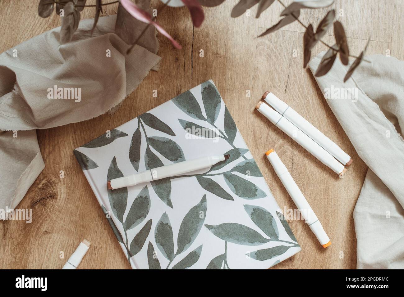 Overhead view of a notebook, marker pens, eucalyptus and fabric on a ...