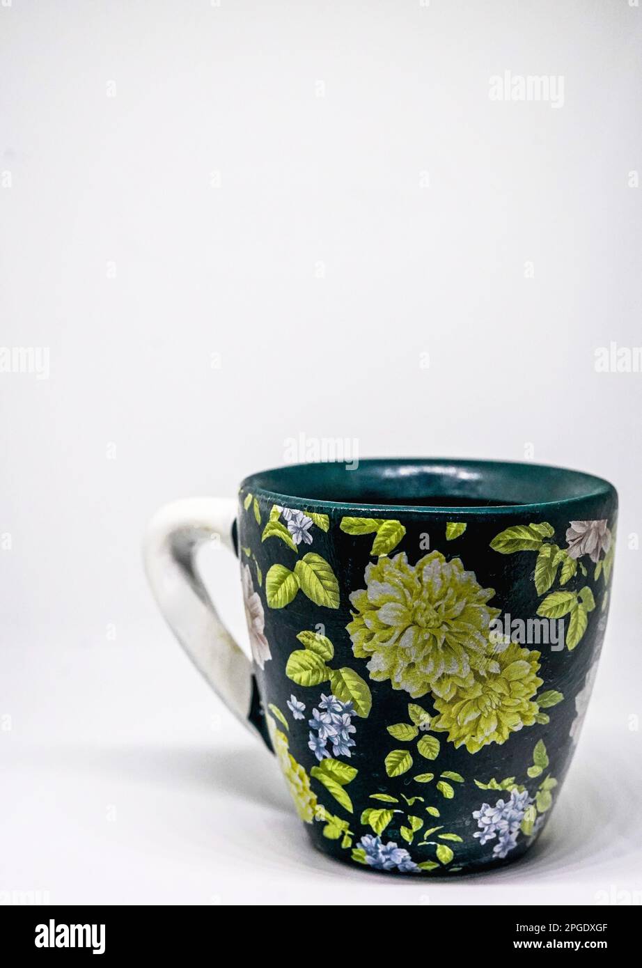 A green ceramic cup with floral patterns is displayed on a white ...