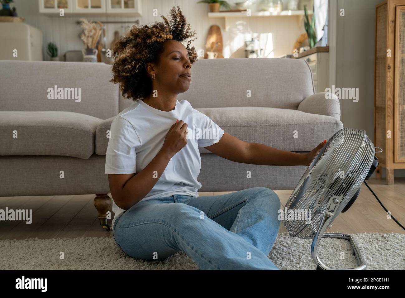 Young African American woman cooling down by ventilator at home ...