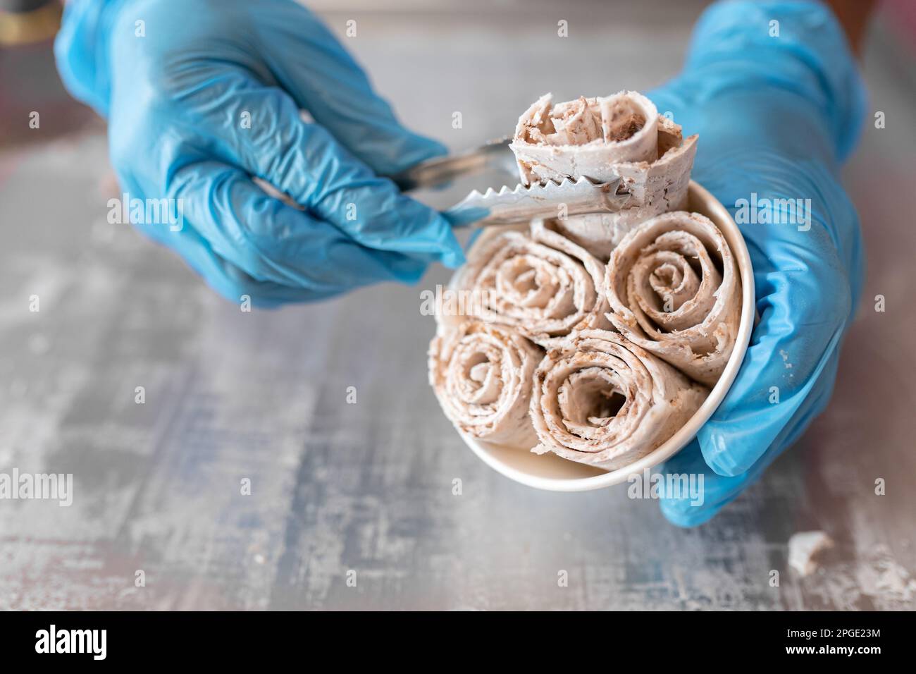 A worker is putting chocolate ice cream rolls in a tub using tongs and ...