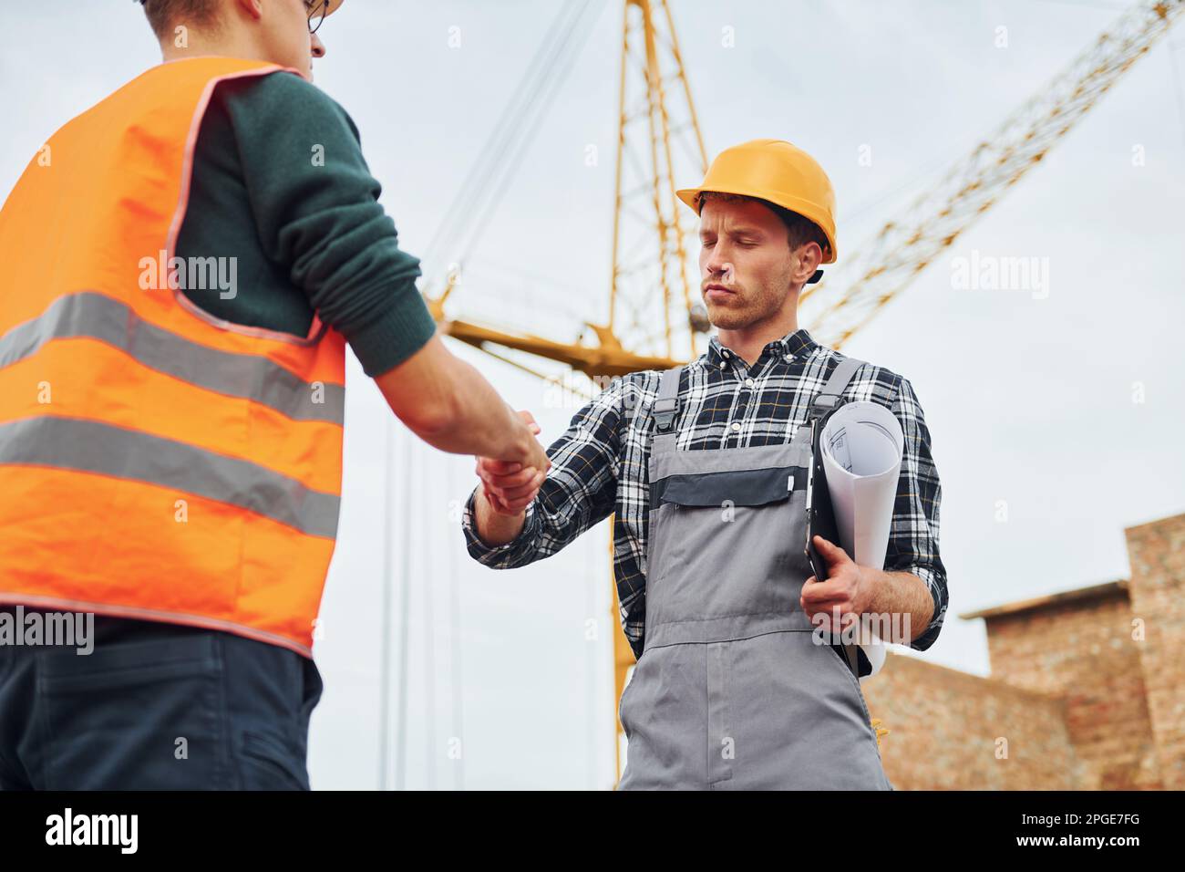 Making handshake. Two construction workers in uniform and safety ...