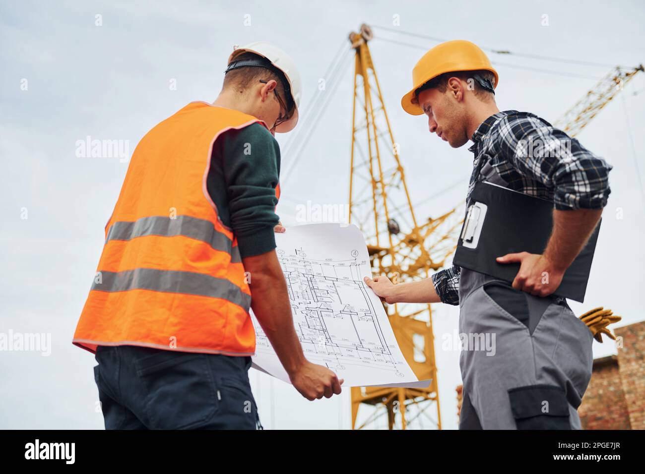 Using paper document with plan on it. Two construction workers in ...