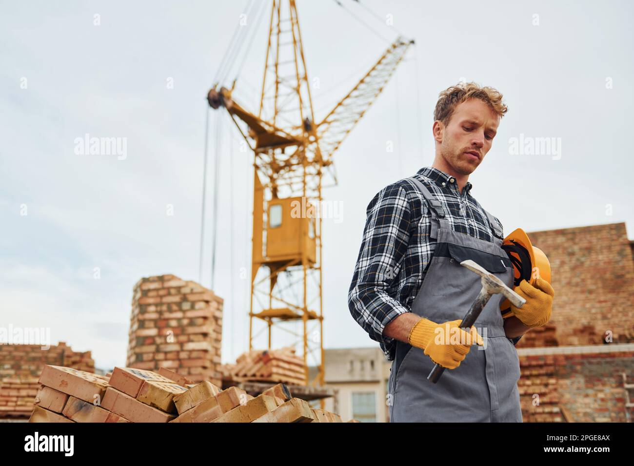 Standing and holds hard hat with hammer. Construction worker in uniform ...