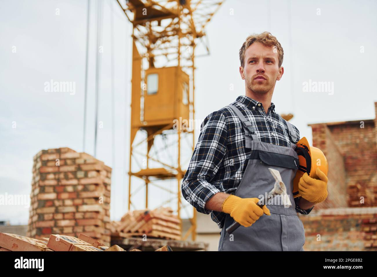 Standing and holds hard hat with hammer. Construction worker in uniform ...