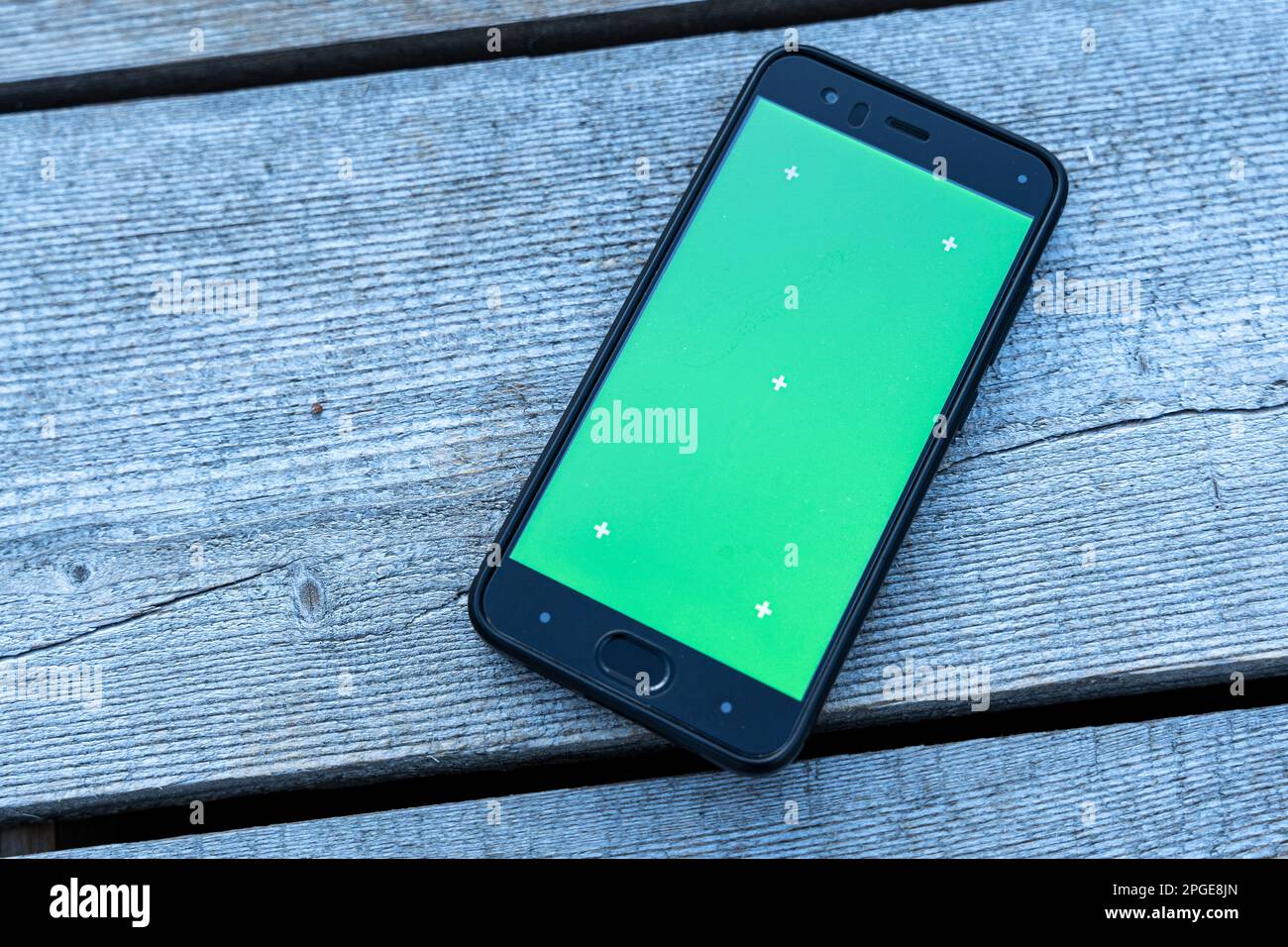 a smartphone with a green screen lies on a faded wooden background ...