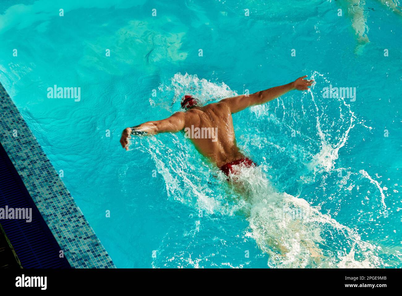 A man swims in the pool in a red cap and glasses among the rays of the ...