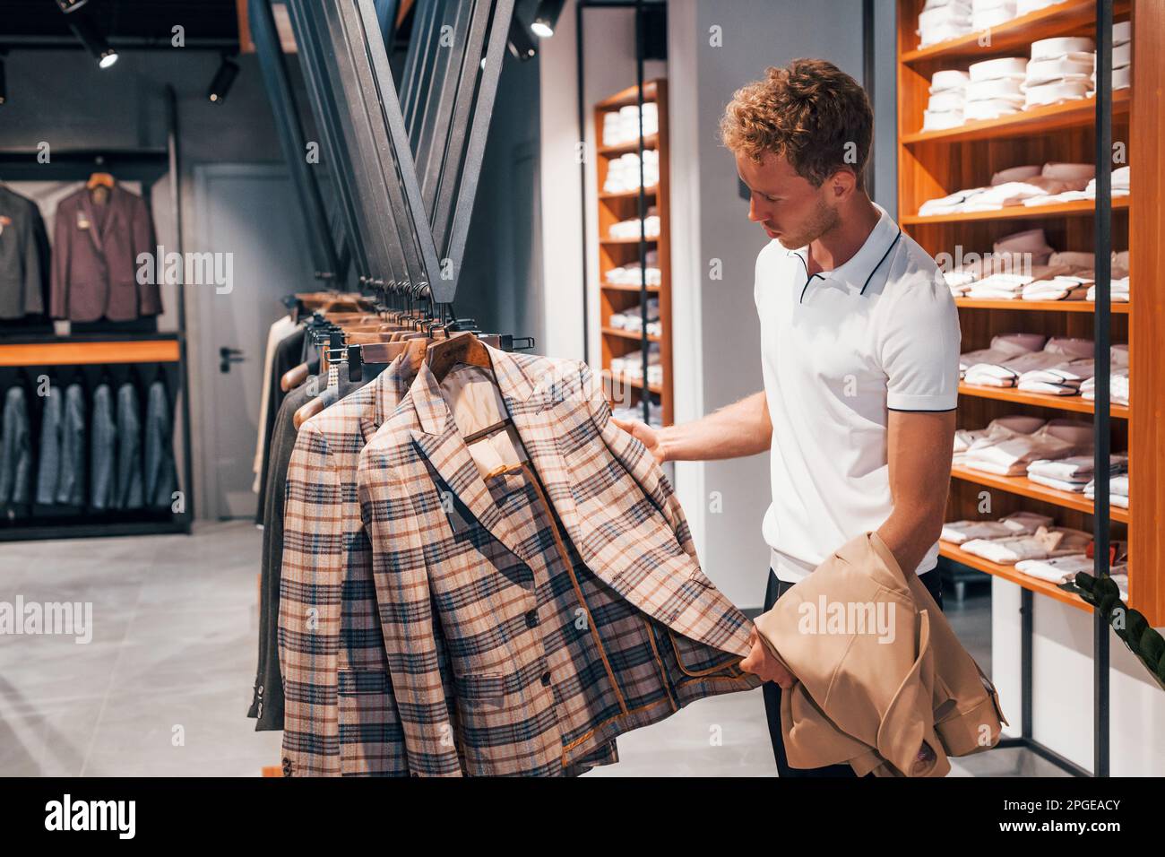 Looks for jacket. Young guy in modern store with new clothes. Elegant ...