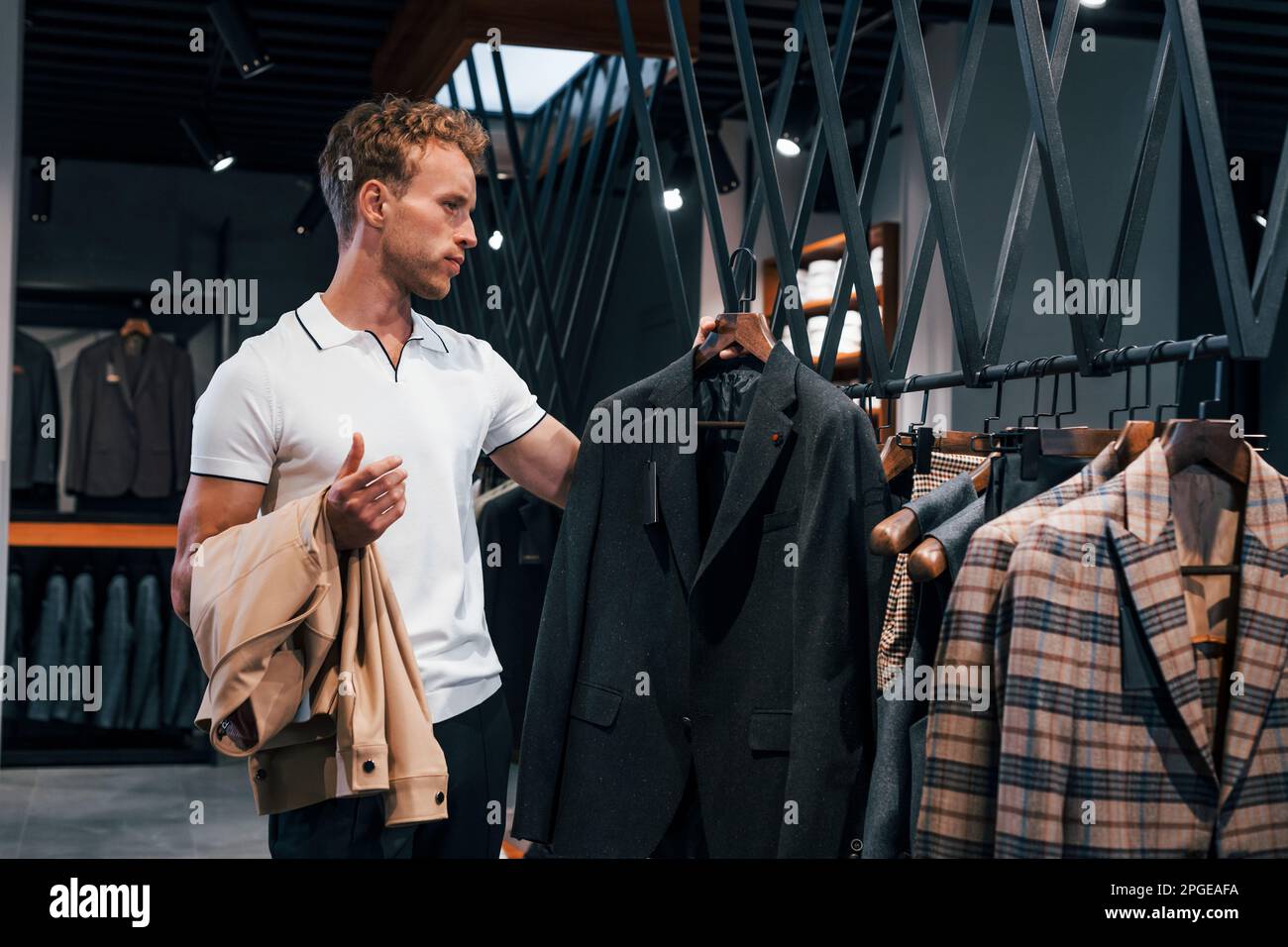 Looks for jacket. Young guy in modern store with new clothes. Elegant ...