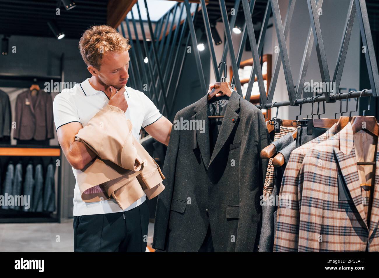 Looks for jacket. Young guy in modern store with new clothes. Elegant ...