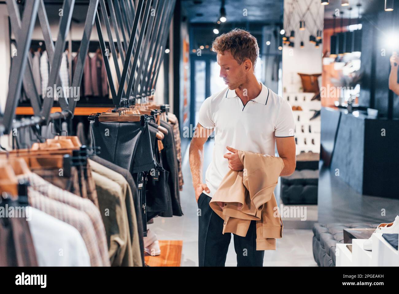 Looks for jacket. Young guy in modern store with new clothes. Elegant ...