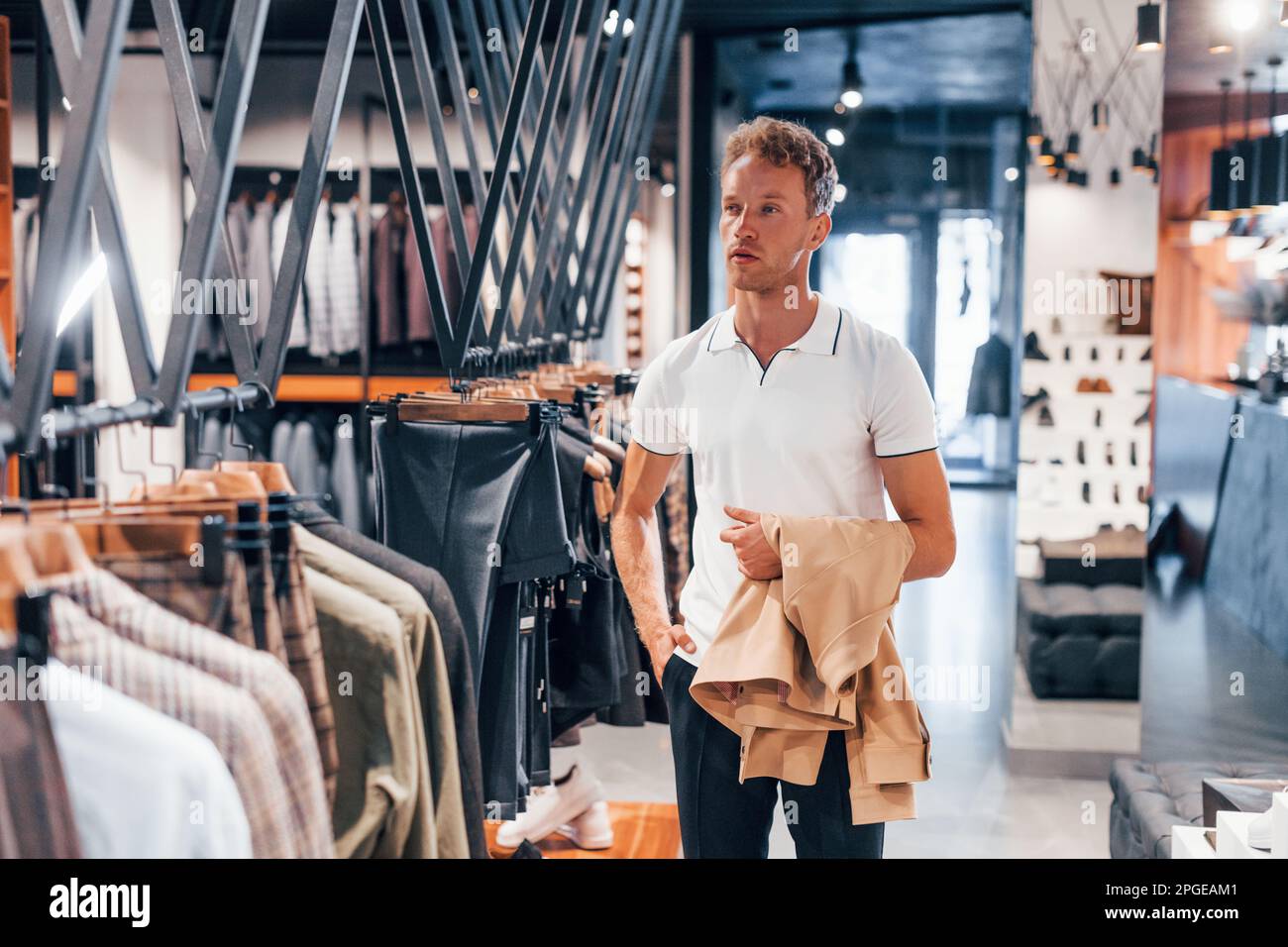 Looks for jacket. Young guy in modern store with new clothes. Elegant ...