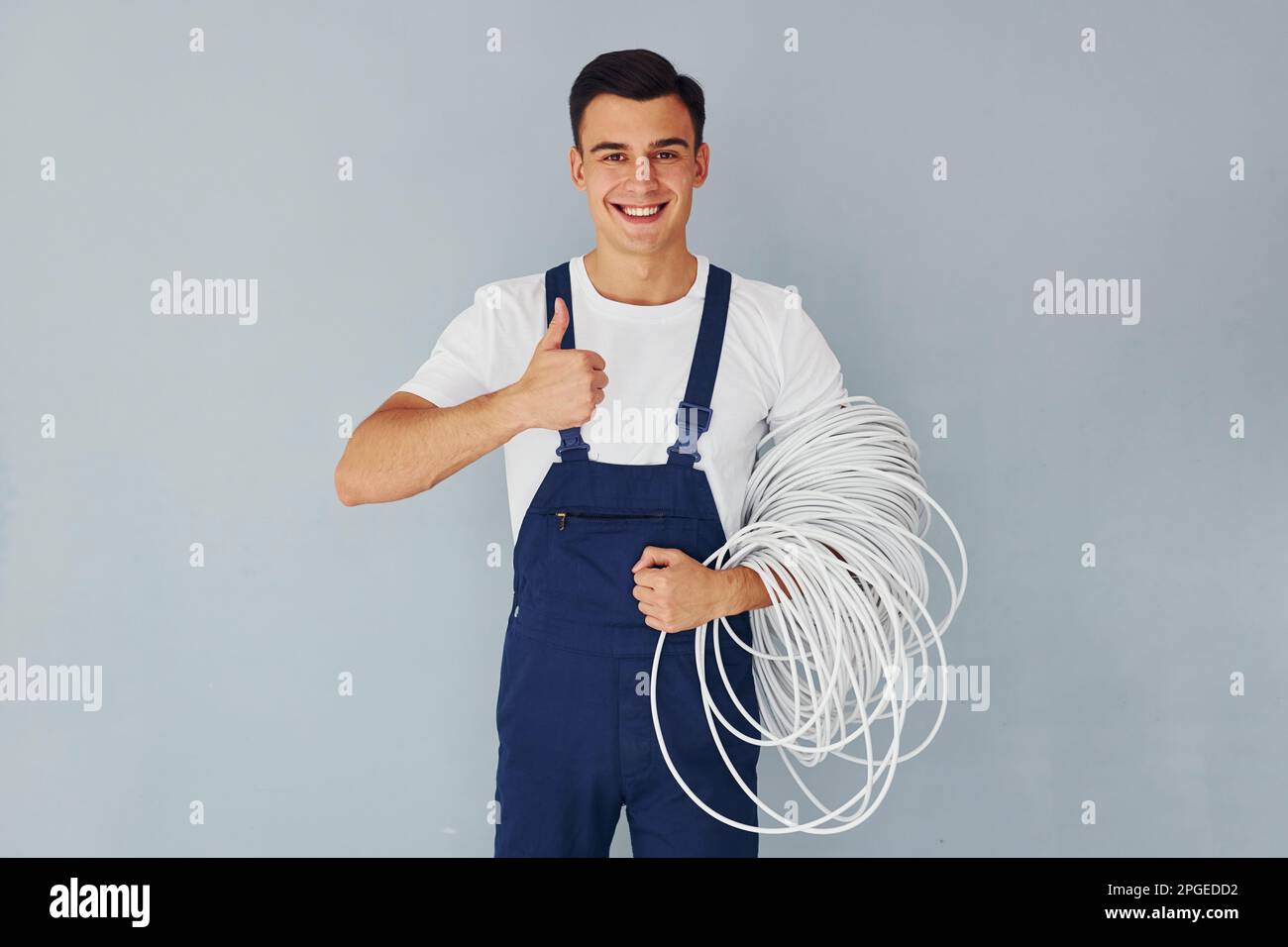 Holds cable. Male worker in blue uniform standing inside of studio ...