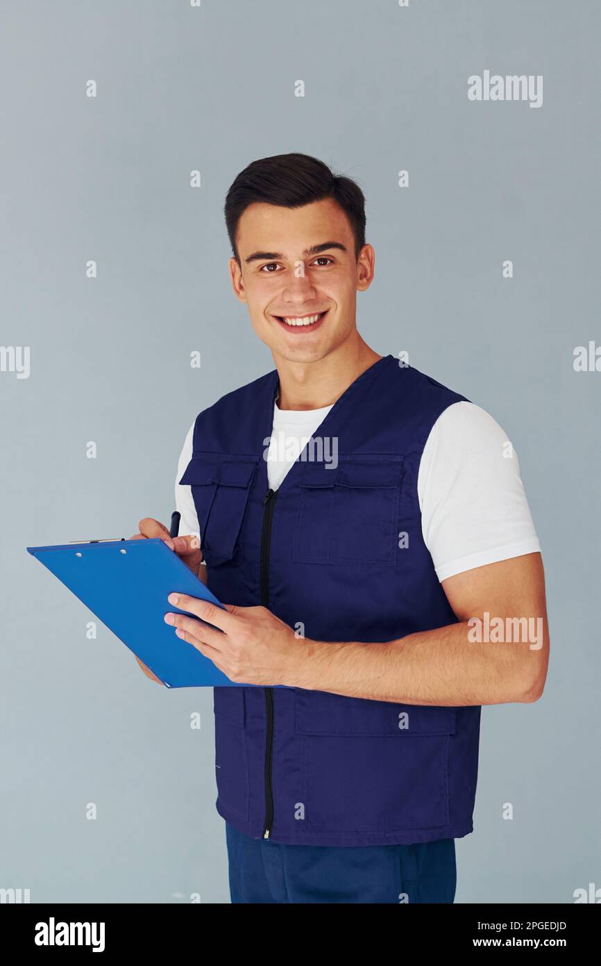Writes in notepad. Male worker in blue uniform standing inside of ...