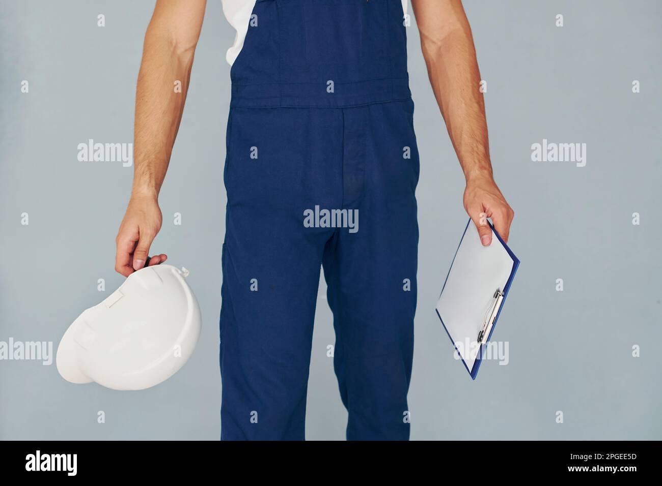With notepad and hard hat. Male worker in blue uniform standing inside ...
