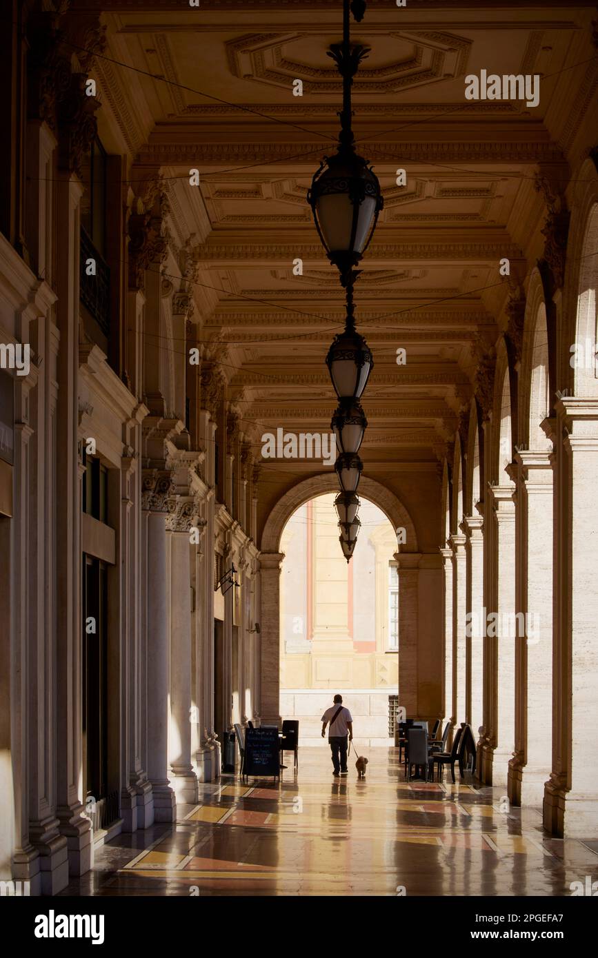Man walking dog through arched walkway of Palazzo della Regione Liguria ...