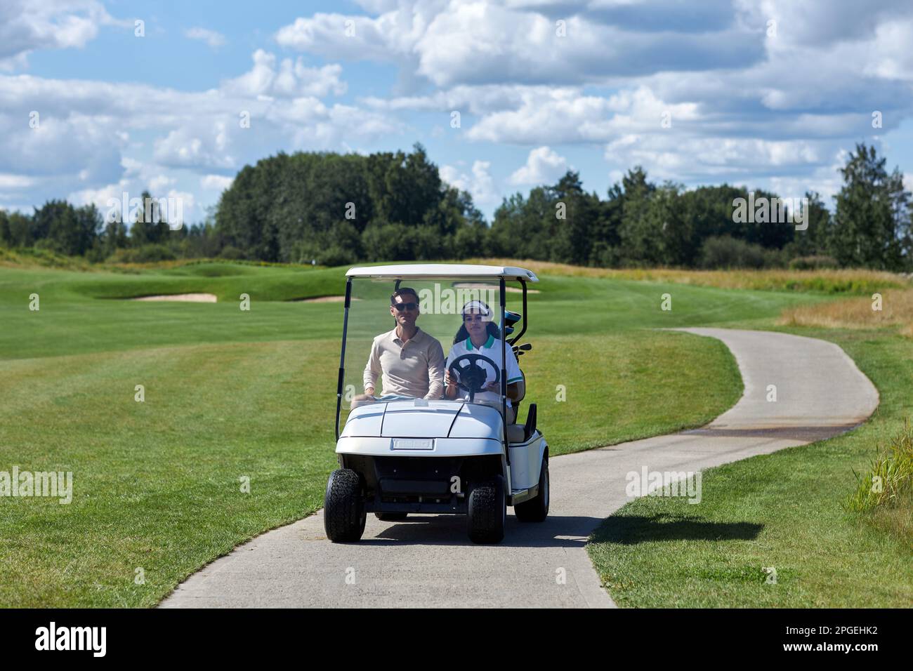 Front view of couple driving golf cart on road towards camera across ...