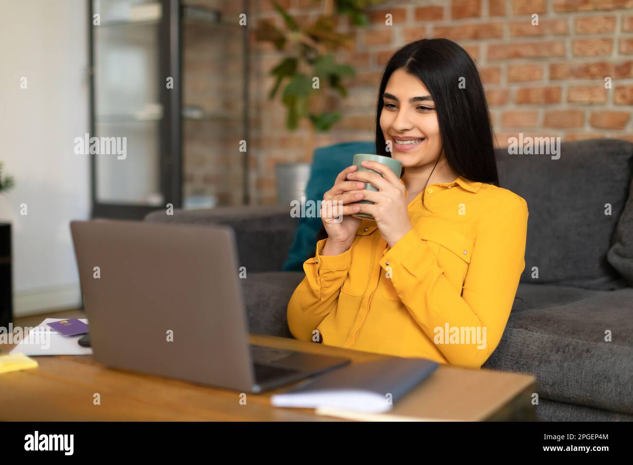 Positive spanish lady watching videos on Internet and drinking coffee ...