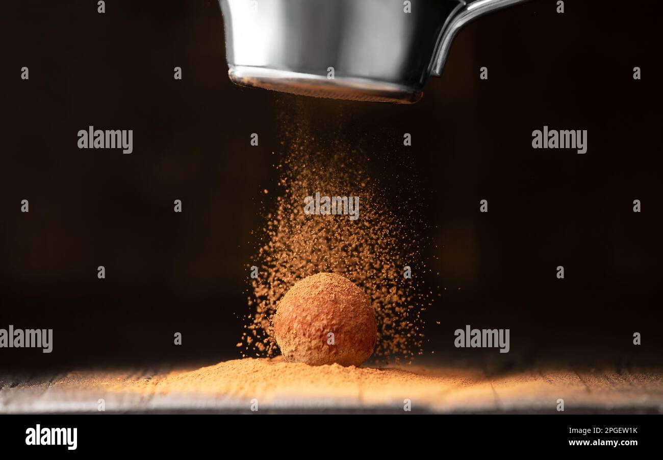 A ball of chocolate truffle is sprinkled with cocoa from a strainer on ...