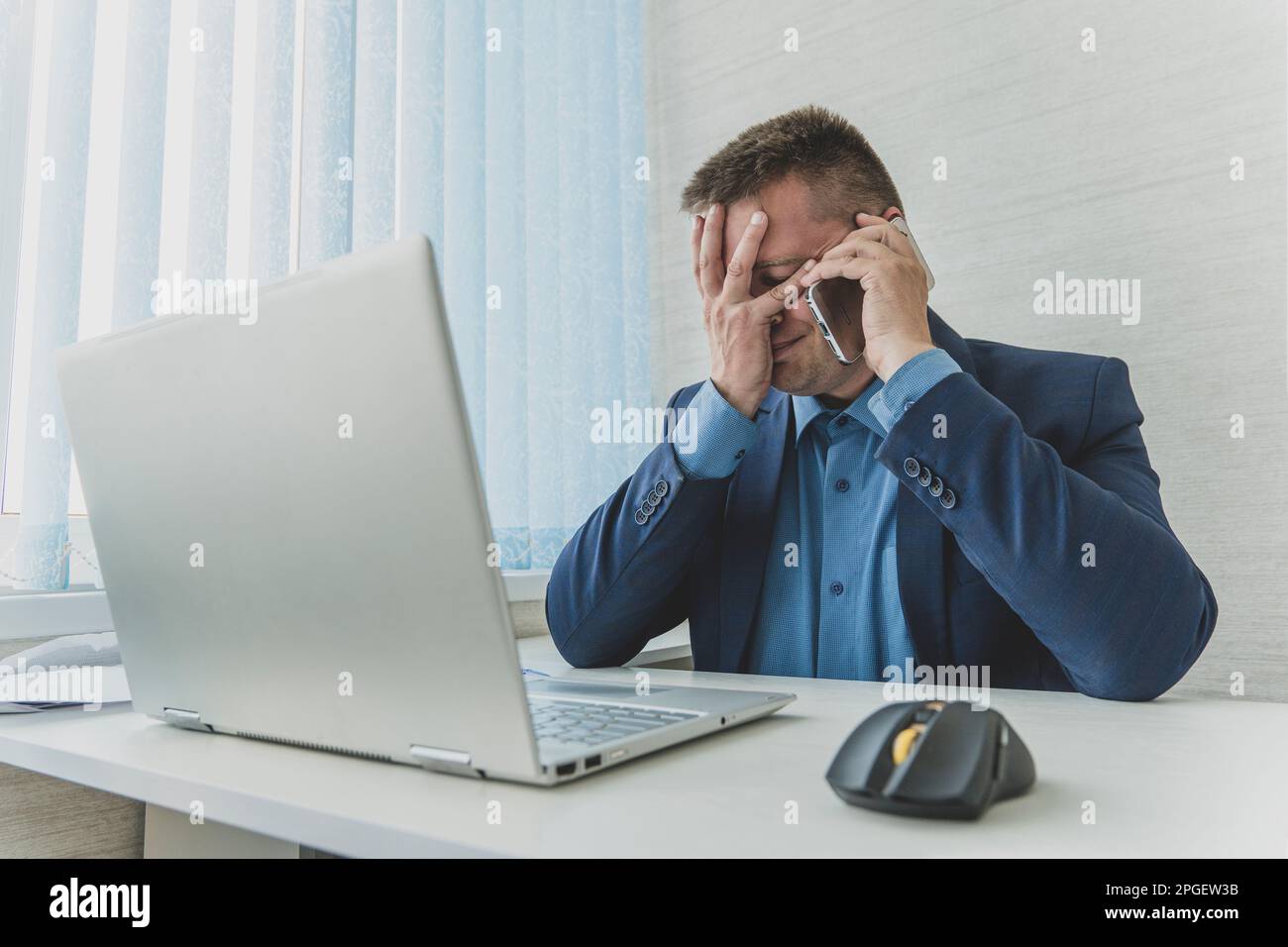 Tired or exhausted man closing his face with hands sitting in front of ...
