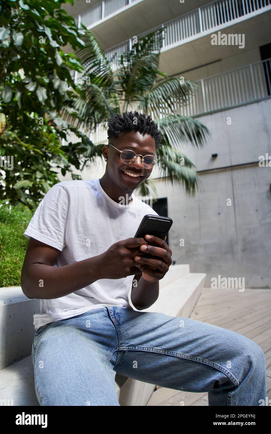 Vertical portrait smiling black boy using cell phone campus. Cheerful ...