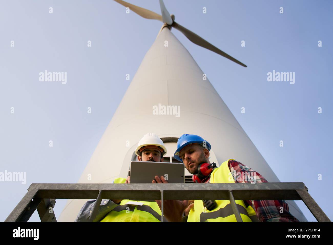 Two helmeted engineers using and looking tablet. Professional technical ...