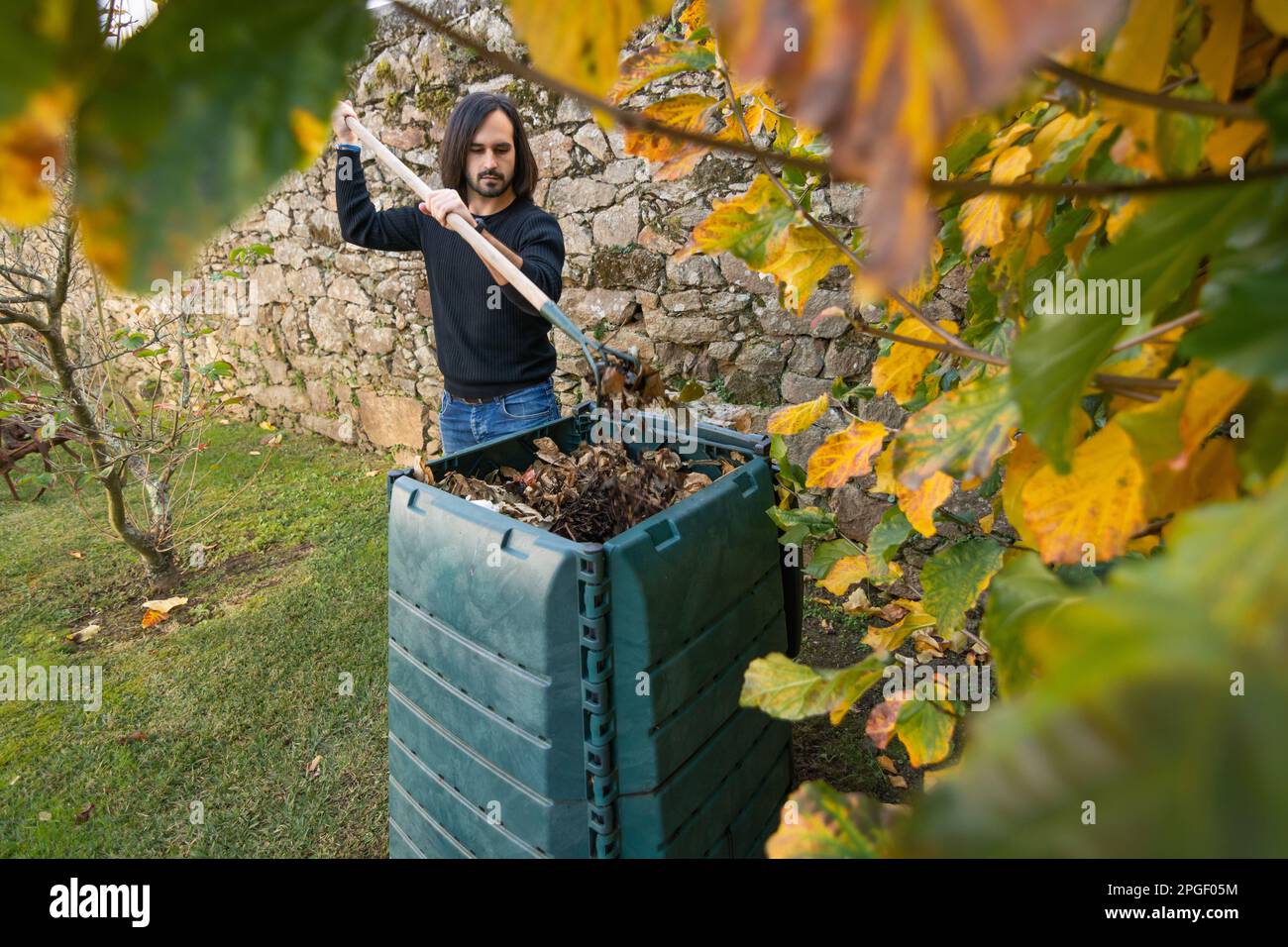 A man is mixing the organic waste with dry leaves in a outdoor compost ...