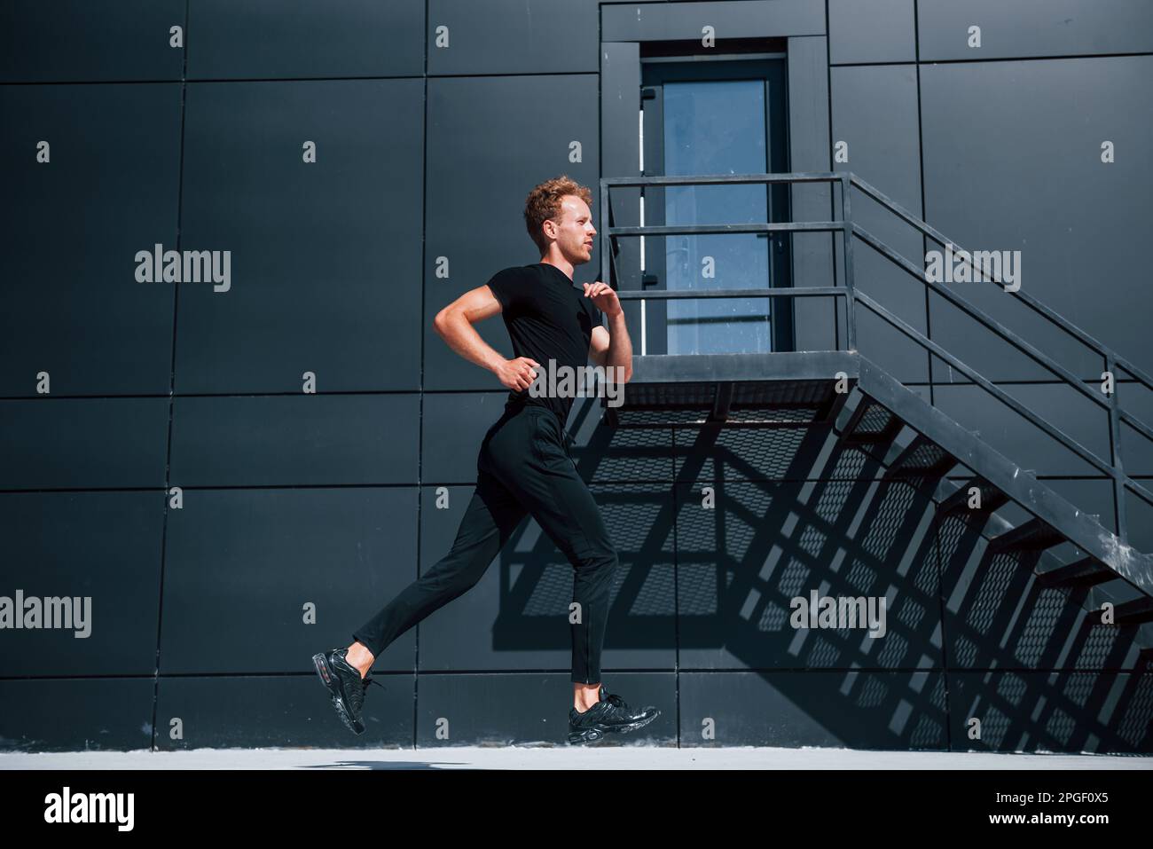 Running near black building. Sportive young guy in black shirt and ...