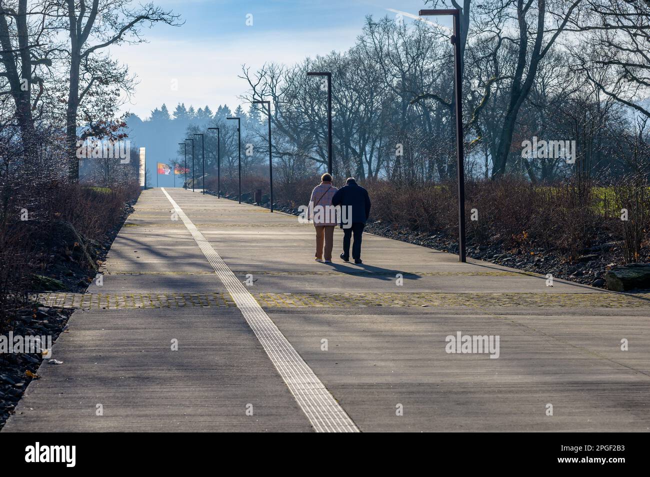 Caucasian elderly couple walking arm in arm down a public park pathway ...