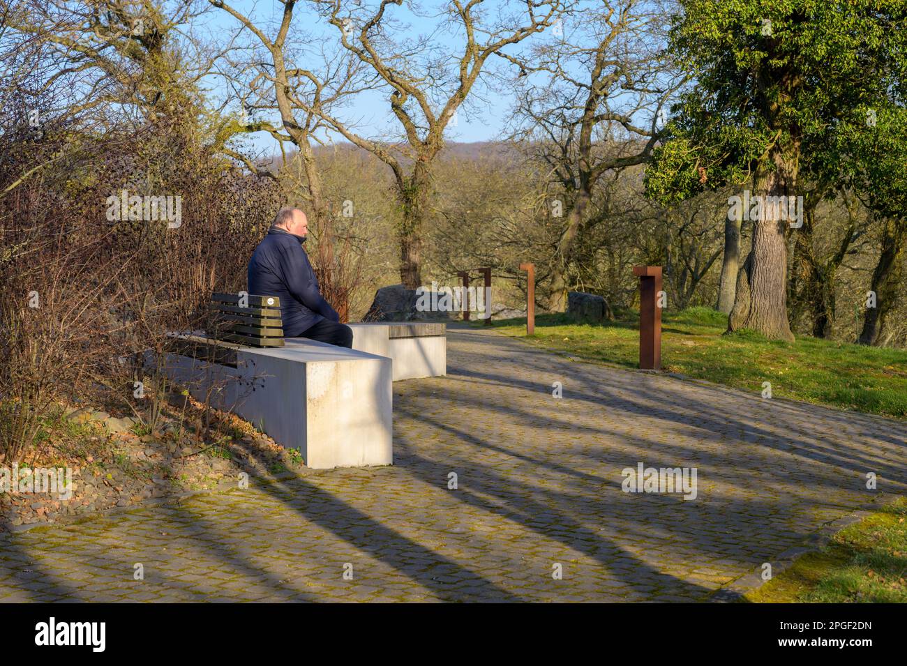 A senior man sits alone on a bench in a park looking into the distance ...