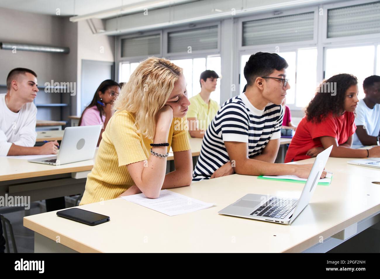 Bored student attending in class with a laptop at high school classroom. Group of students of a ...