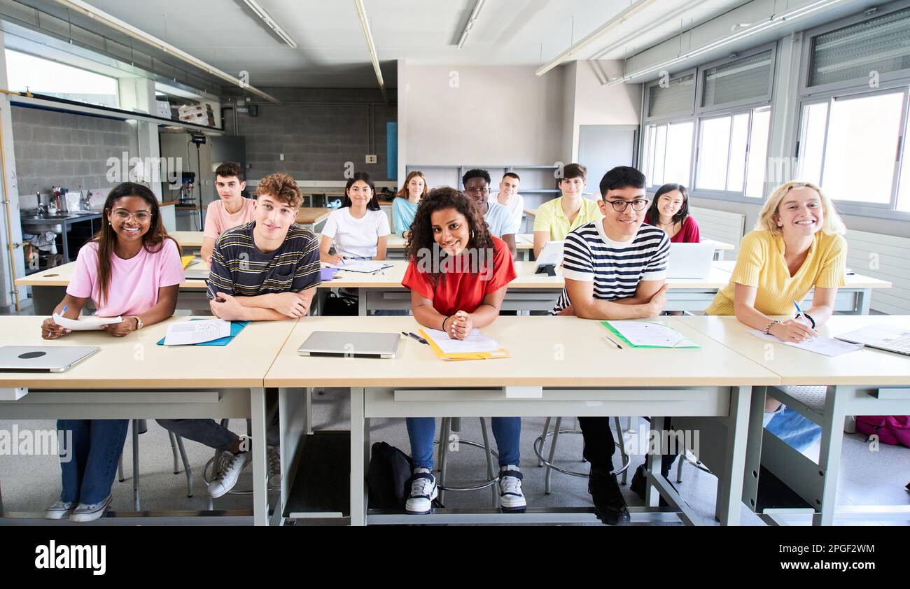 Smiling group of university college sitting at classroom looking at ...