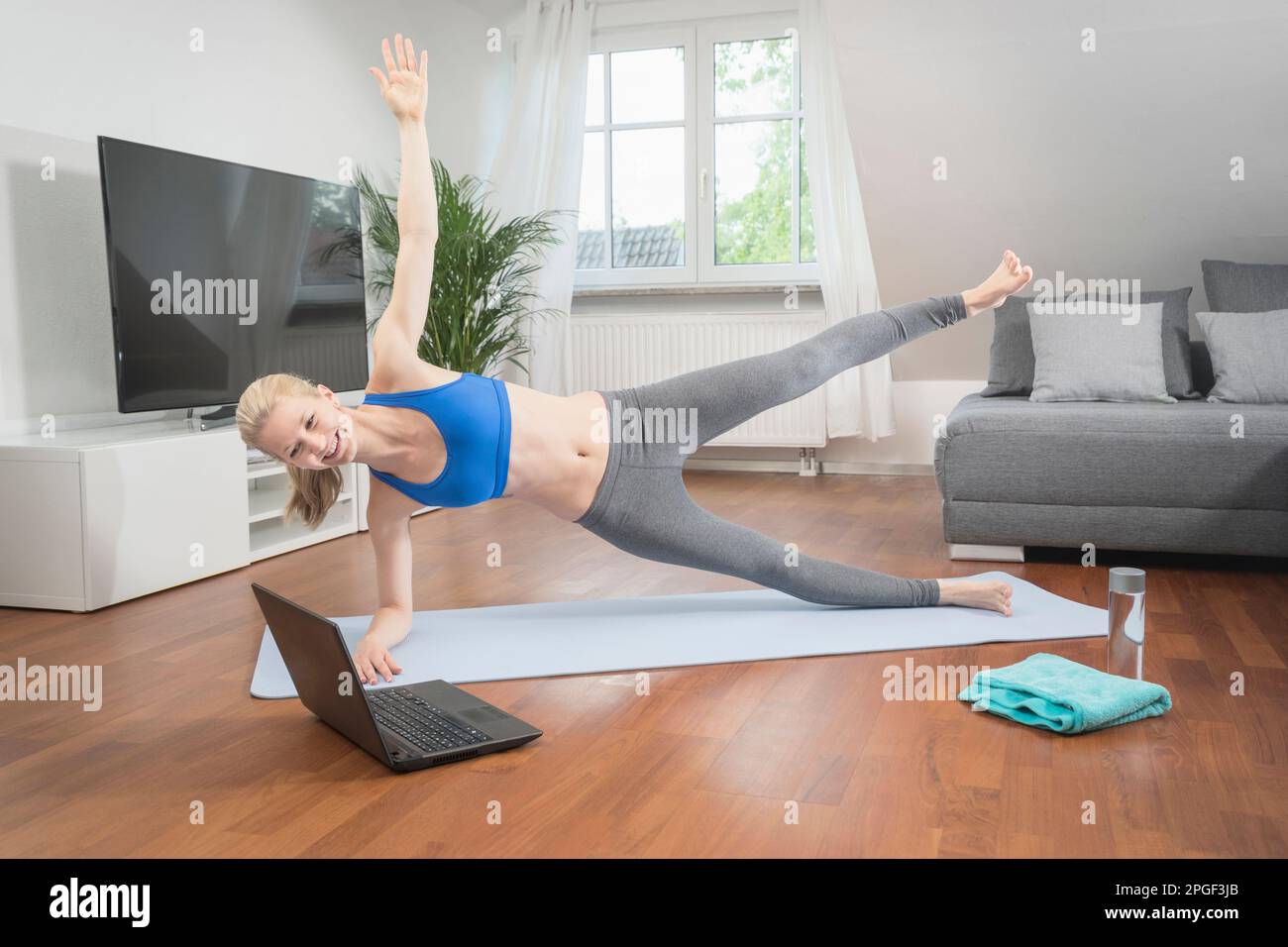 Young woman with laptop doing half moon position on exercise mat in ...