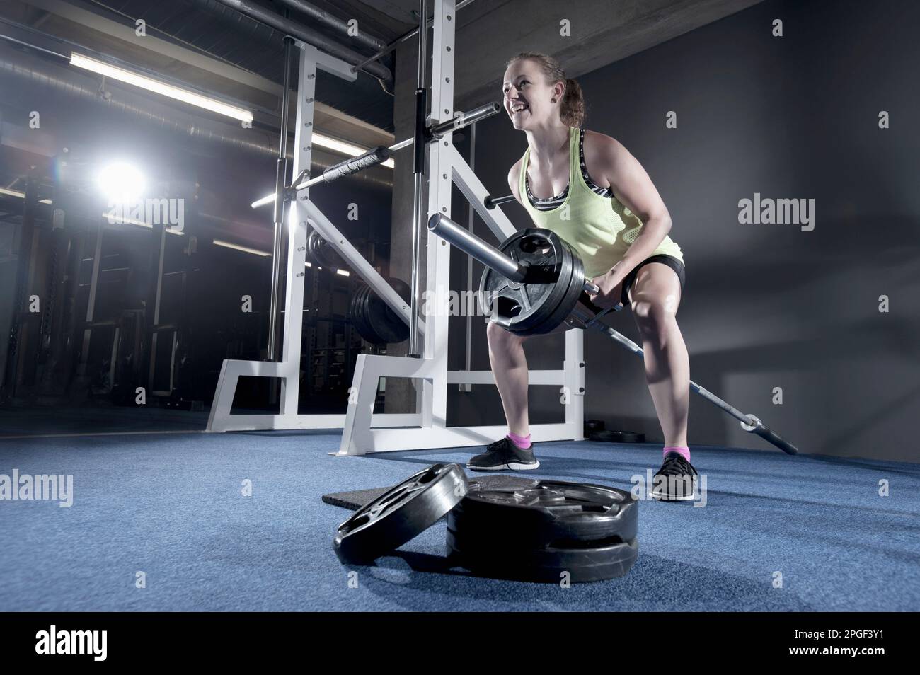 Young woman doing bent over row exercising with long barbell in the gym ...