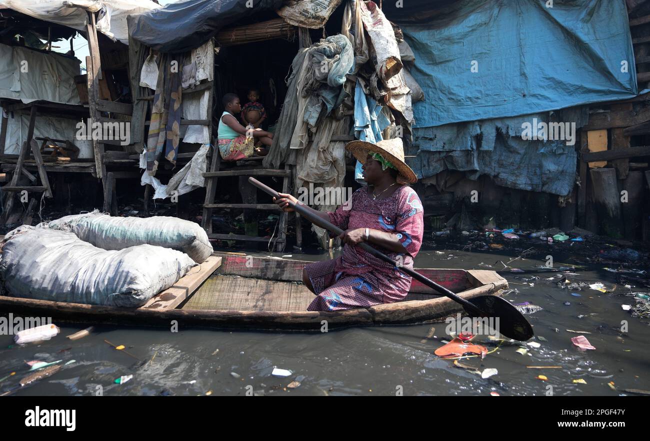 A woman paddles through water surrounded by garbage in a floating slum ...