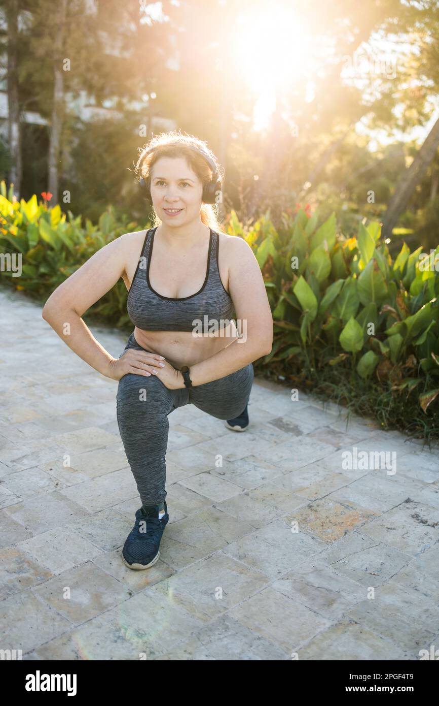 Adorable fat woman in tracksuit is engaged in fitness outdoor side view ...