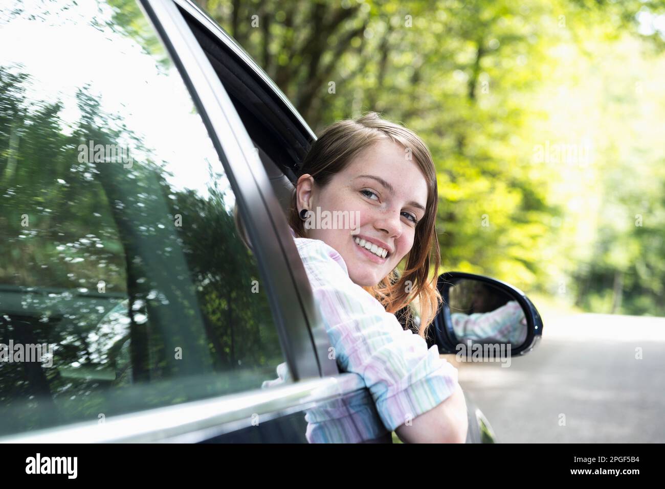 Young woman looking out of car window and smiling, Bavaria, Germany ...