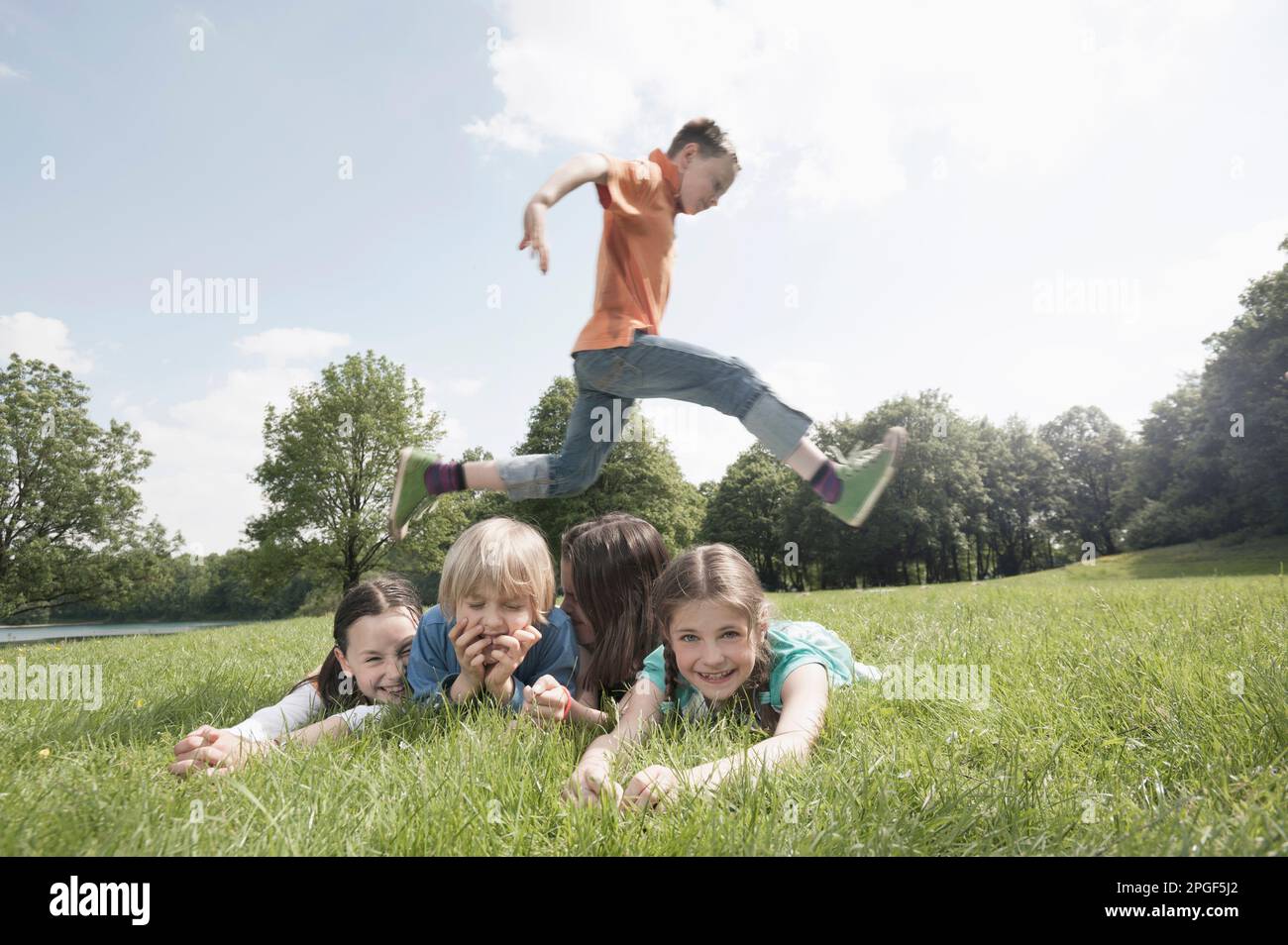 Boy jumping over his friends lying on grass in a park, Munich, Bavaria ...