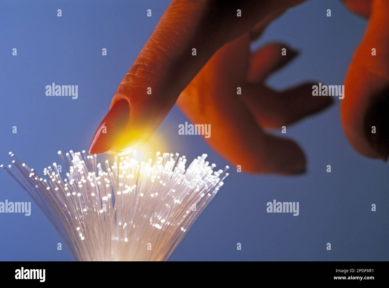 WOMANS INDEX FINGER TIP TOUCHES LIT TIPS OF FIBER OPTIC STRANDS (©KECK ...