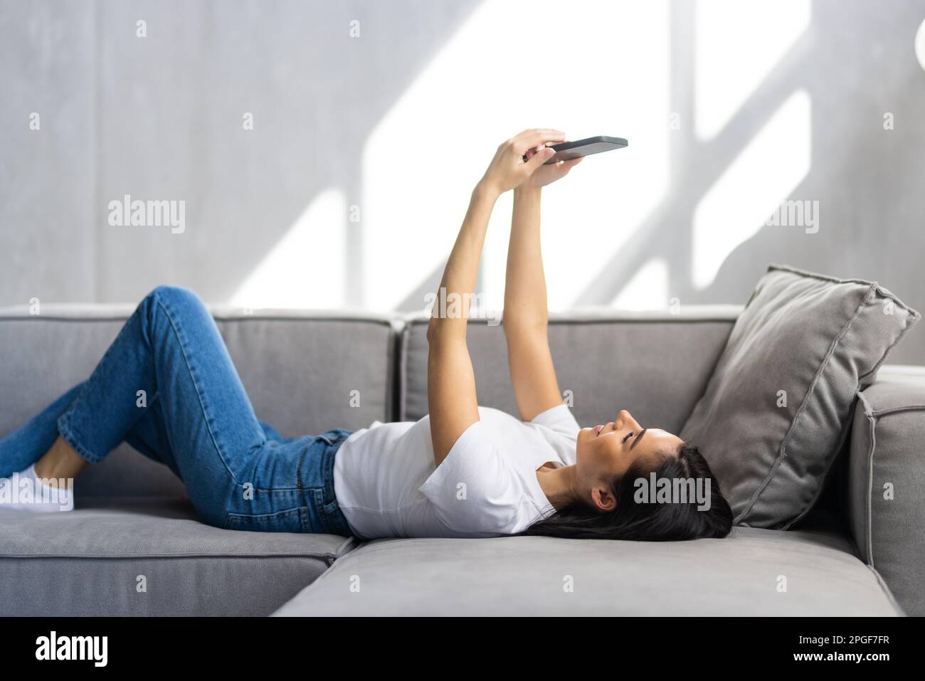 Close up smiling woman lying on couch, using smartphone, happy young female spending leisure ...