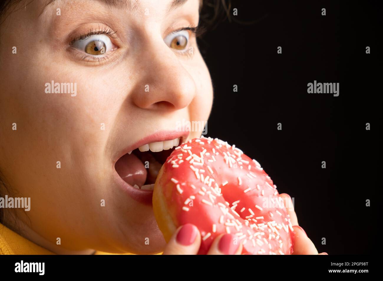 A woman bites a large red donut, a black background, a place for text ...